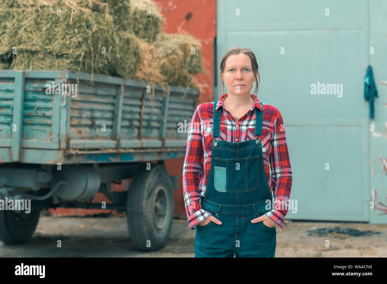 Female farmer posing in front of hay wagon. Portrait of woman farm ...