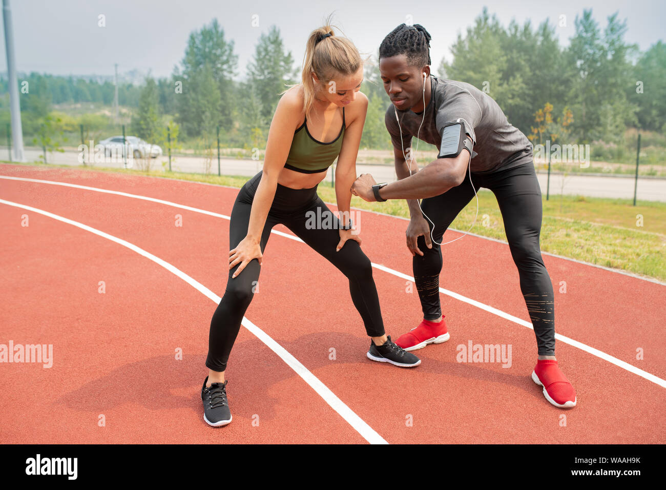 Young athlete showing time to active girl while both standing on start ...