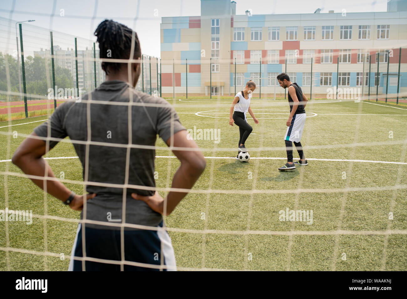 Rear view of young African sportsman standing by net and looking at two ...