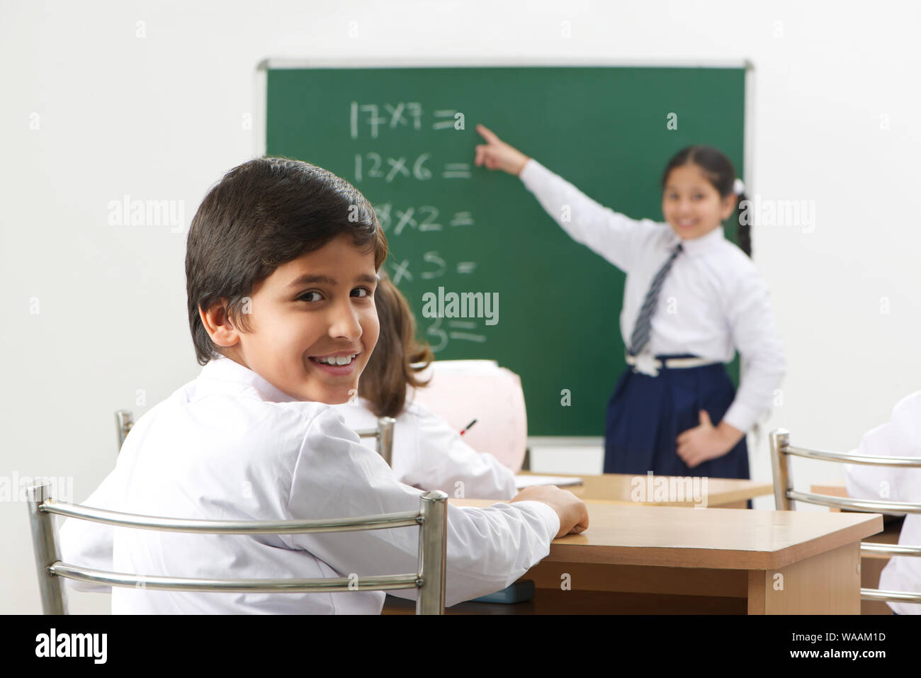 Schoolboy looking back towards camera and schoolgirl teaching her ...