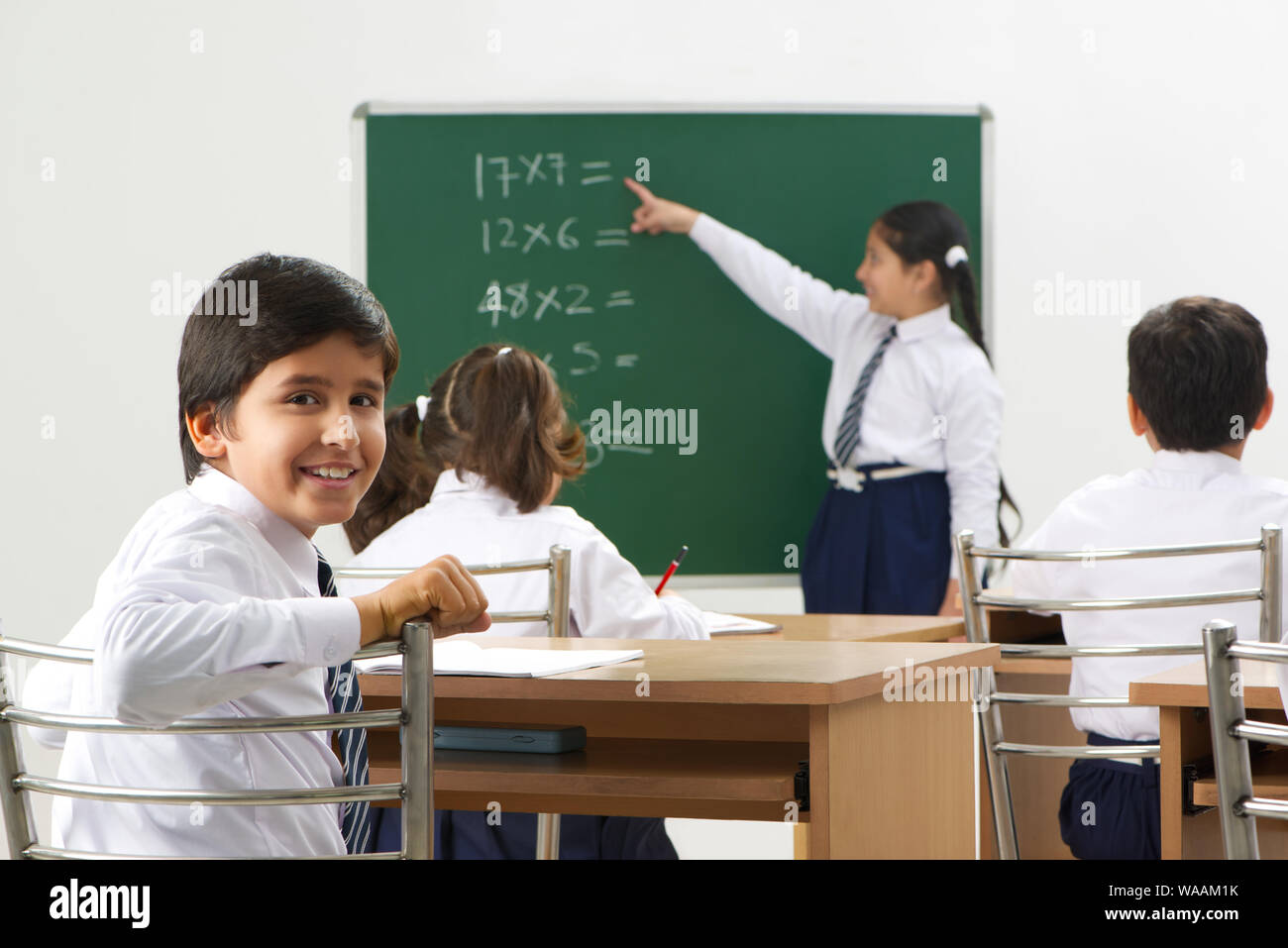 Schoolboy looking back towards camera and schoolgirl teaching her ...