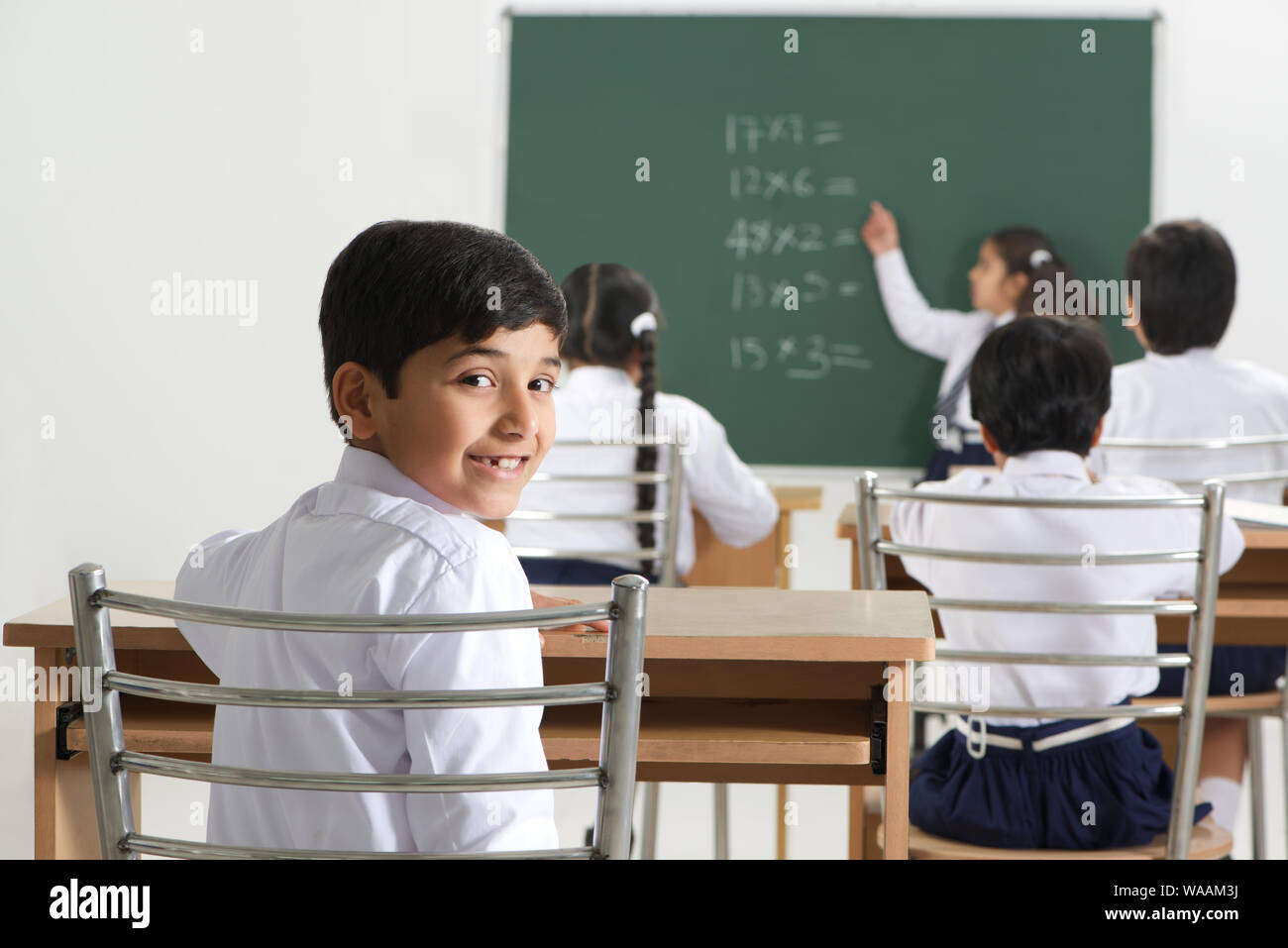 Schoolboy looking back towards camera and schoolgirl teaching her ...
