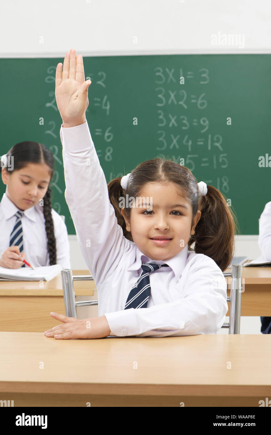 Schoolgirl raising hand in classroom Stock Photo - Alamy