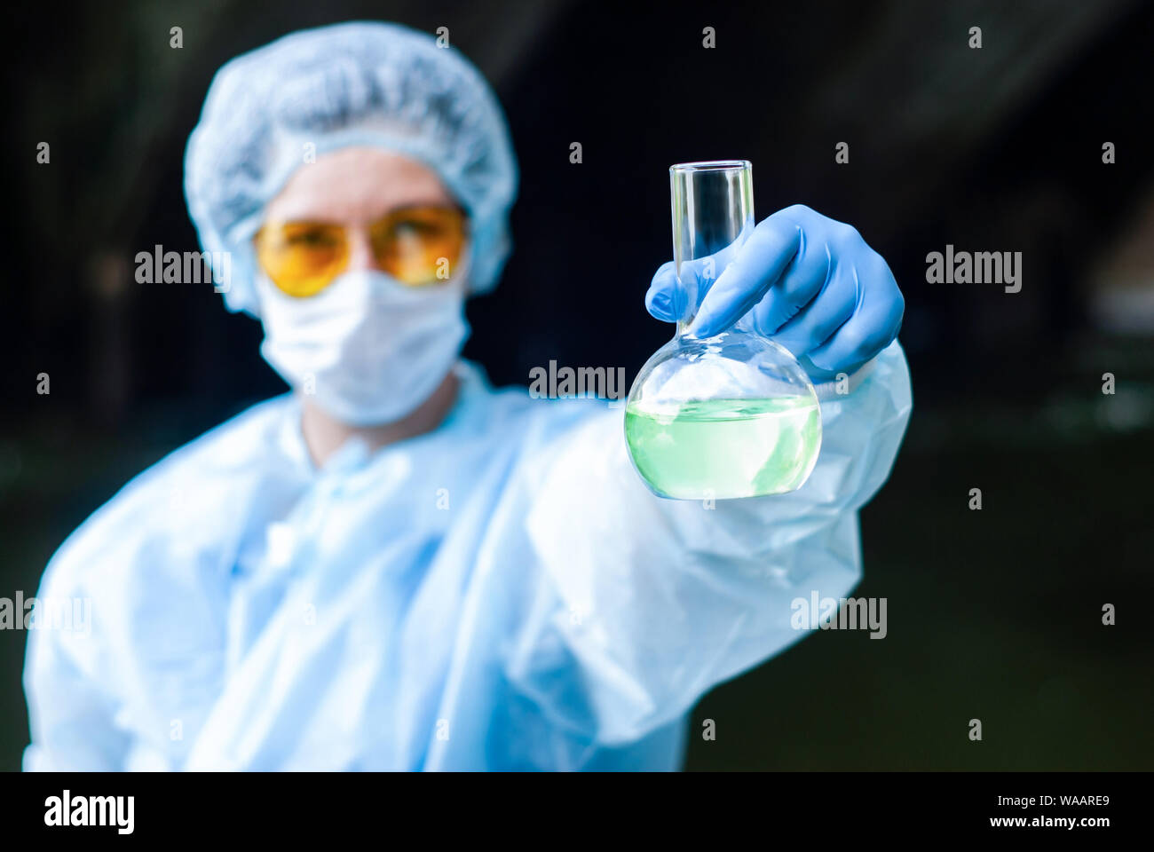 woman in a medical or laboratory suit shows a flask with greenish ...