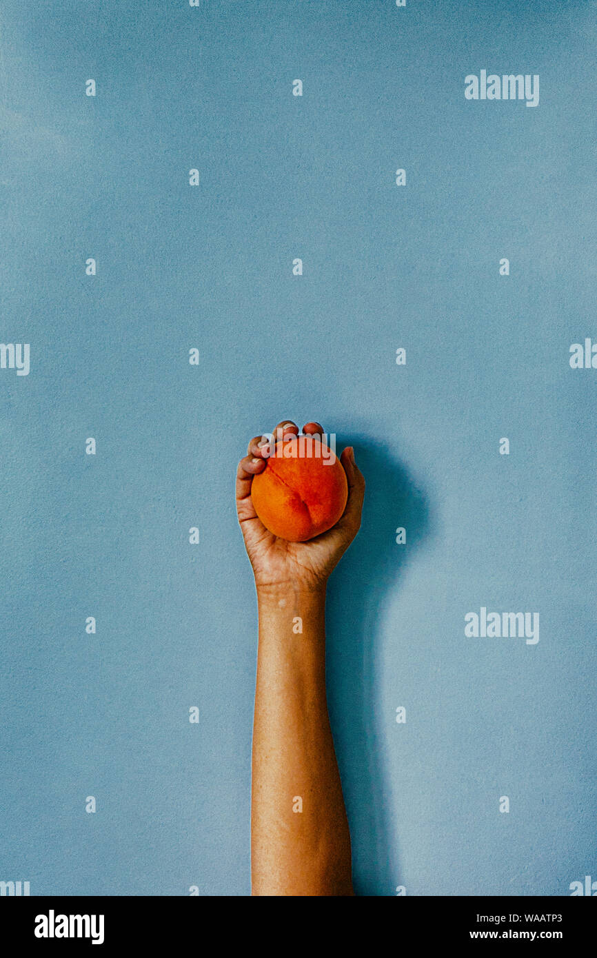 hand hugging a peach on blue wall Stock Photo - Alamy