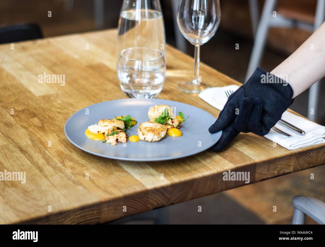 Waiter putting down the dish on a wooden table with a blurred ...