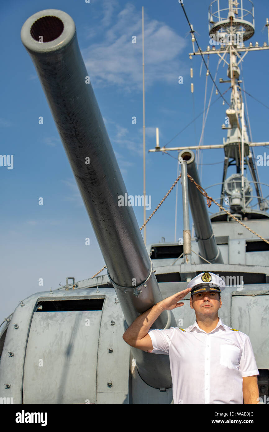A navy officer standing under a ship's cannon and do salute.The captain ...