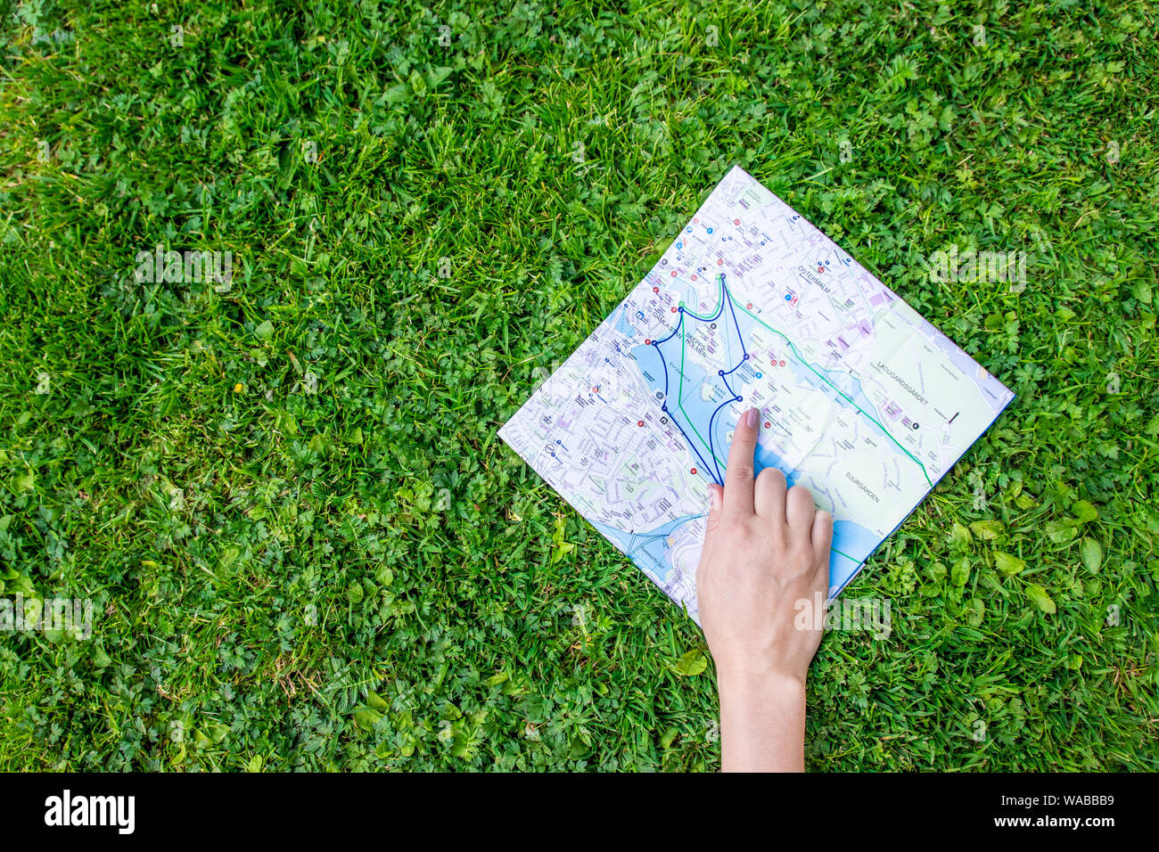 Female hand shows a finger on a topographic map on the grass. Travel on ...