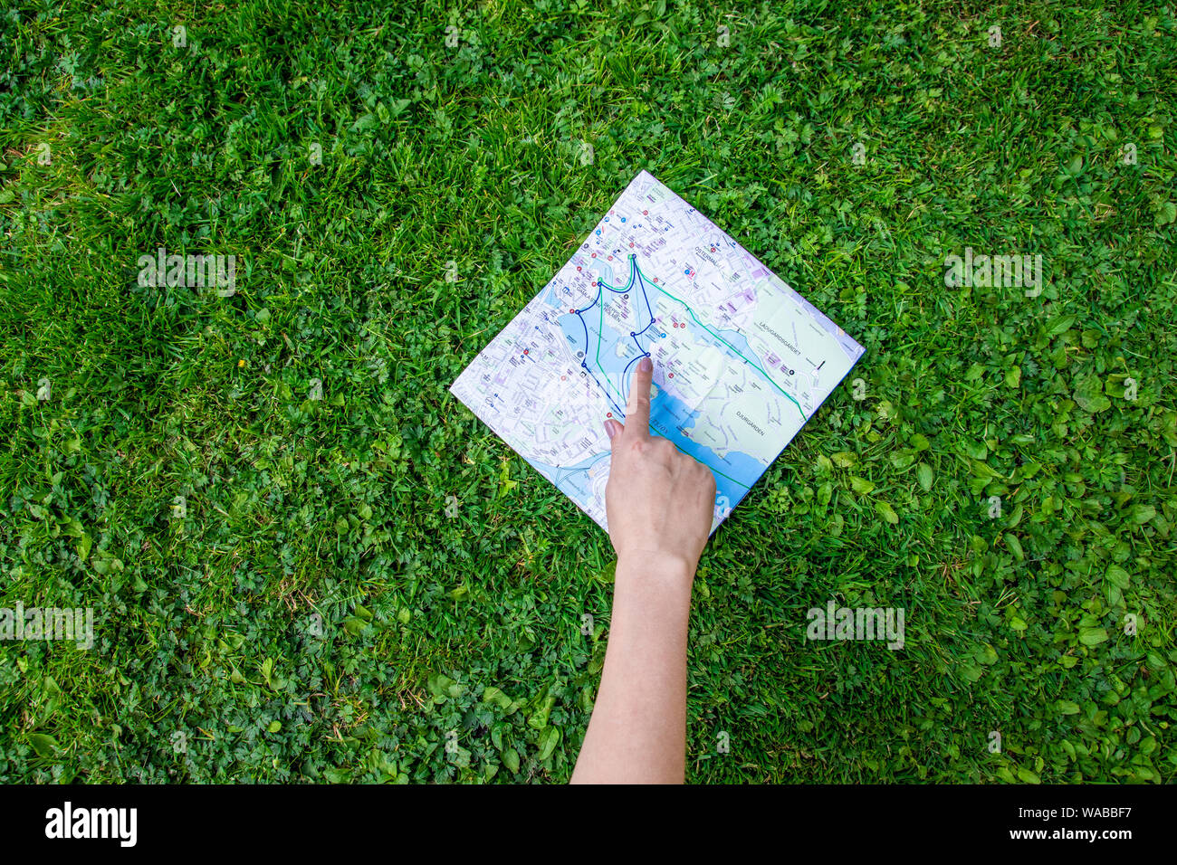 Female hand shows a finger on a topographic map on the grass. Travel on ...