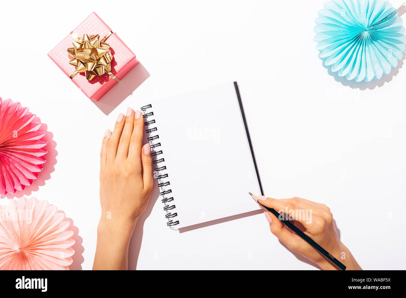 Woman's hands writing in blank notepad near festive bright pink gift ...