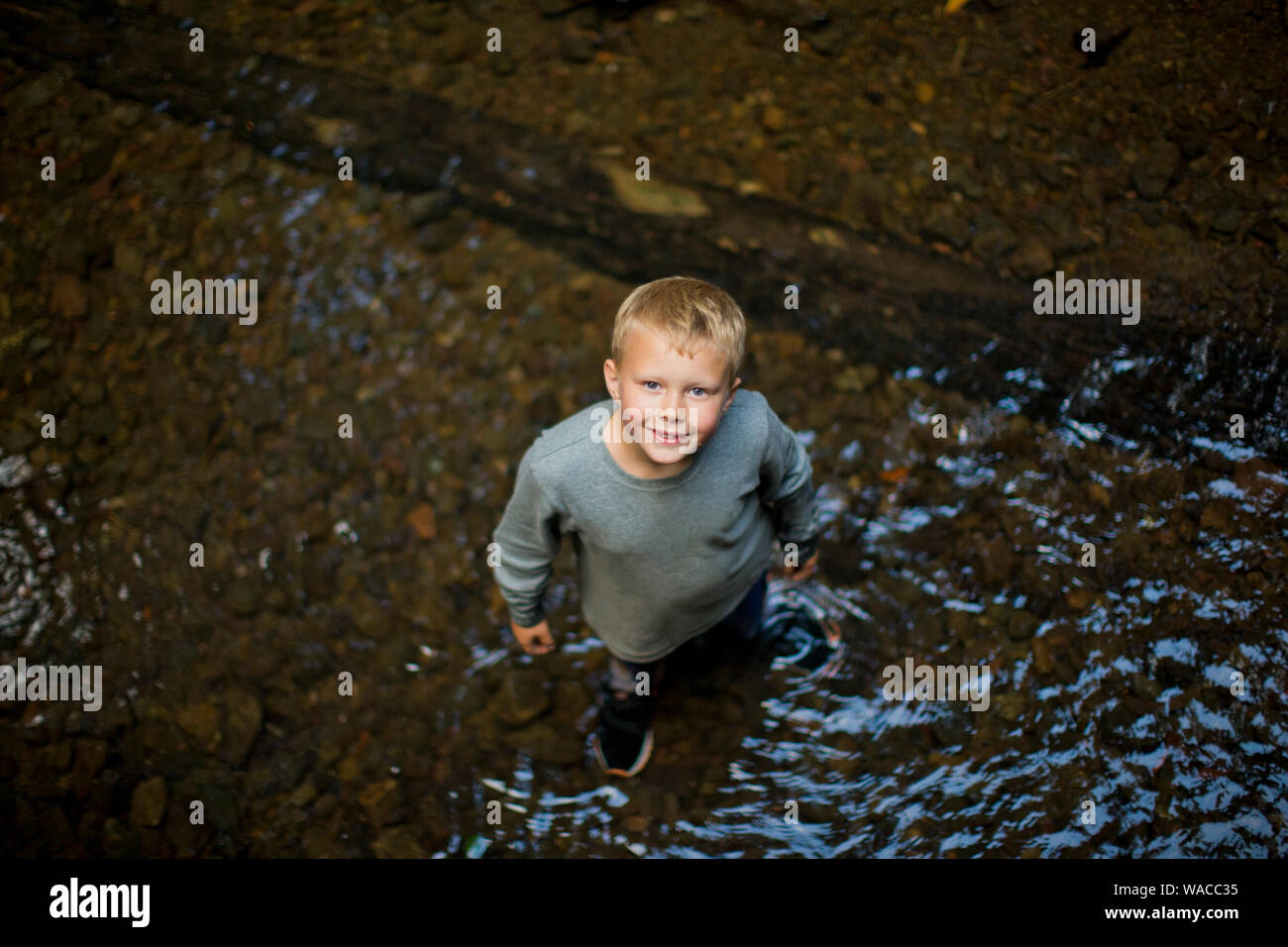 Portrait of young boy looking up while standing in the shallows of a ...