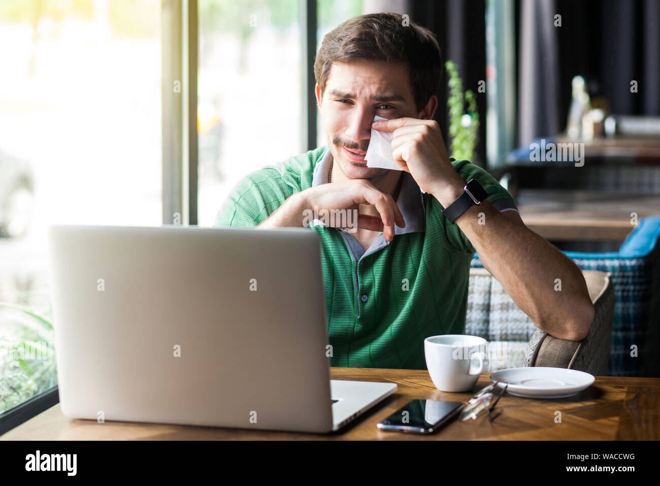 Young sad businessman in green t-shirt sitting, crying and cleaning his ...