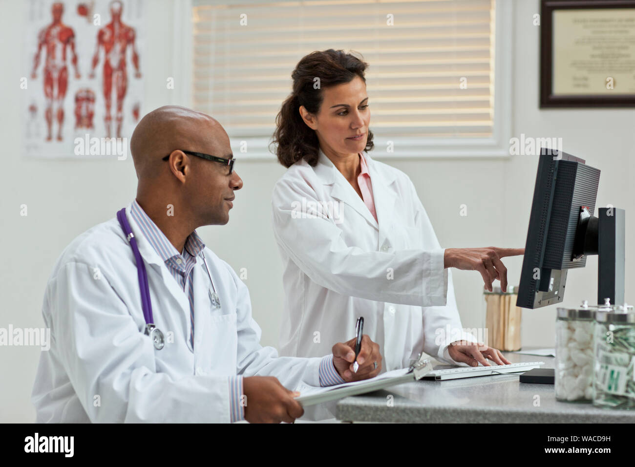Two doctors having a conversation while looking at a computer monitor ...