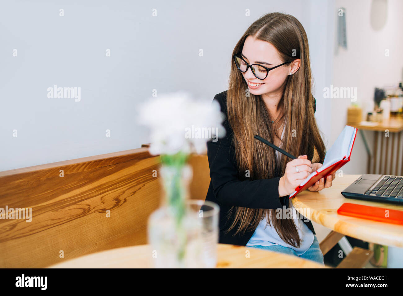 Young happy laughing businesswoman in glasses making notes in her ...
