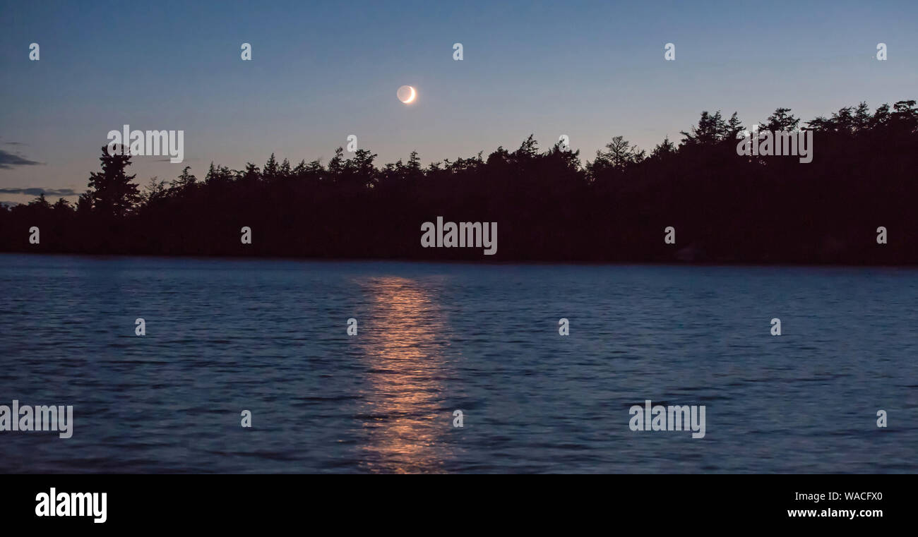 A crescent moon illuminated by the setting sun casts a golden glow over ...