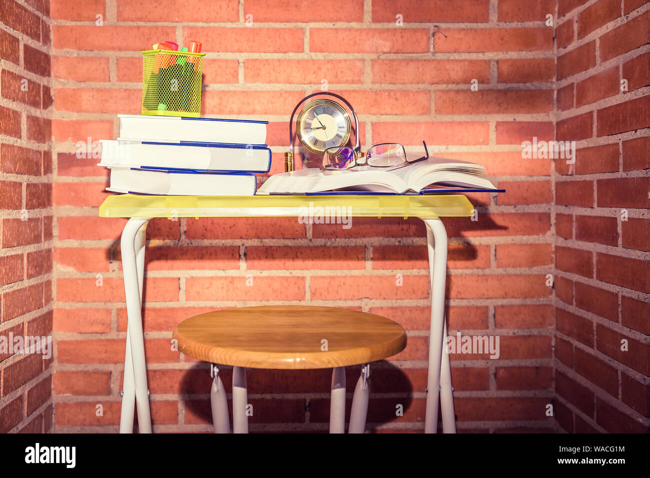 yellow school desk with wooden chair and books in front of a brick wall ...