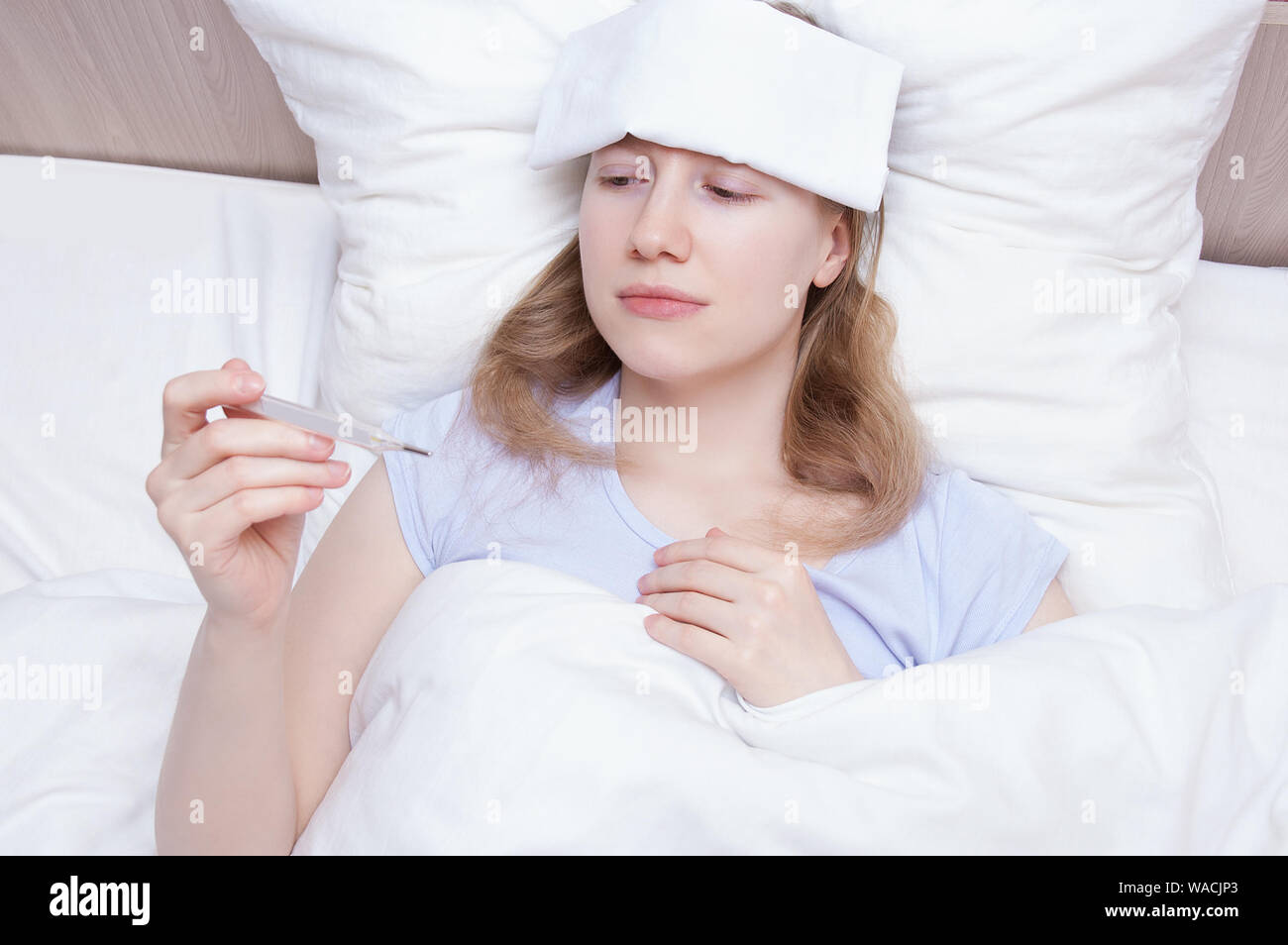 Cold and headache. Caucasian girl lying on the bed with a thermometer ...