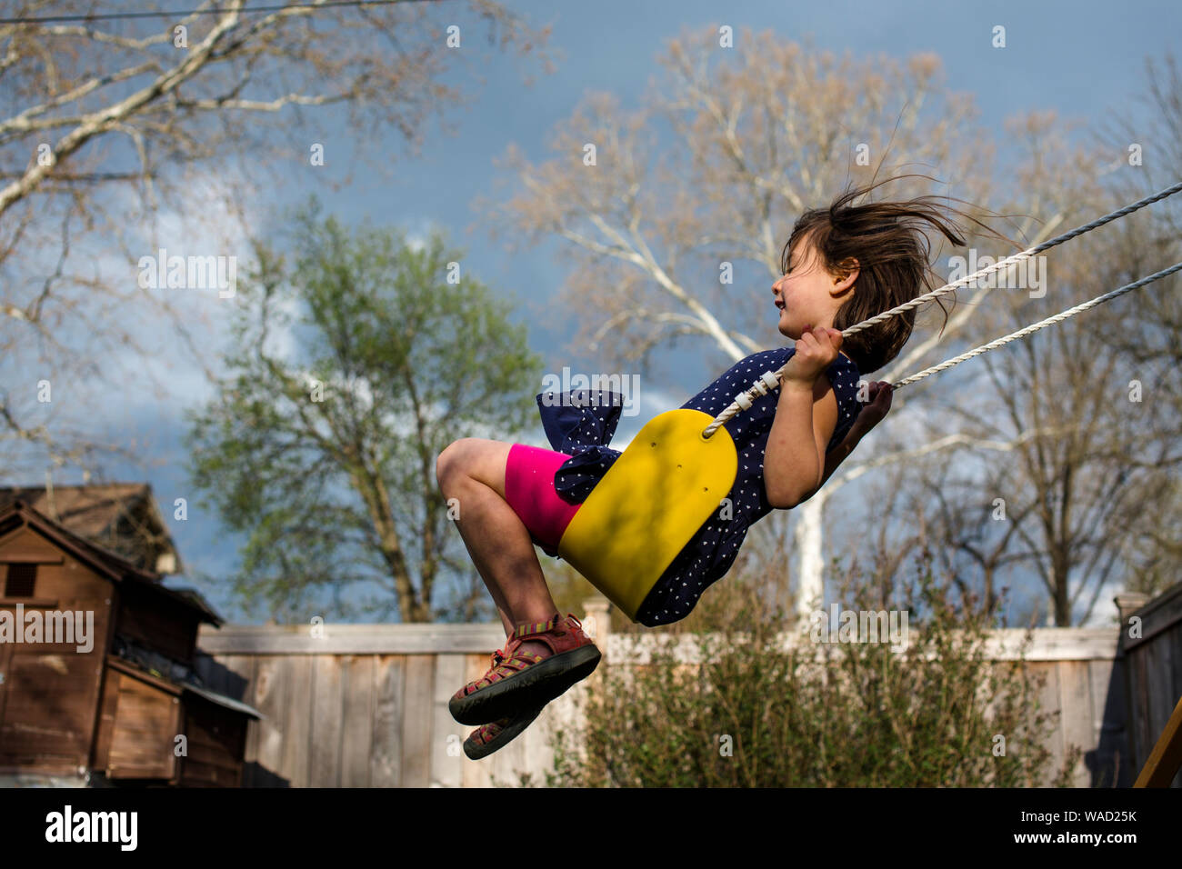 A happy girl on a yellow swing on a breezy, stormy spring day Stock ...