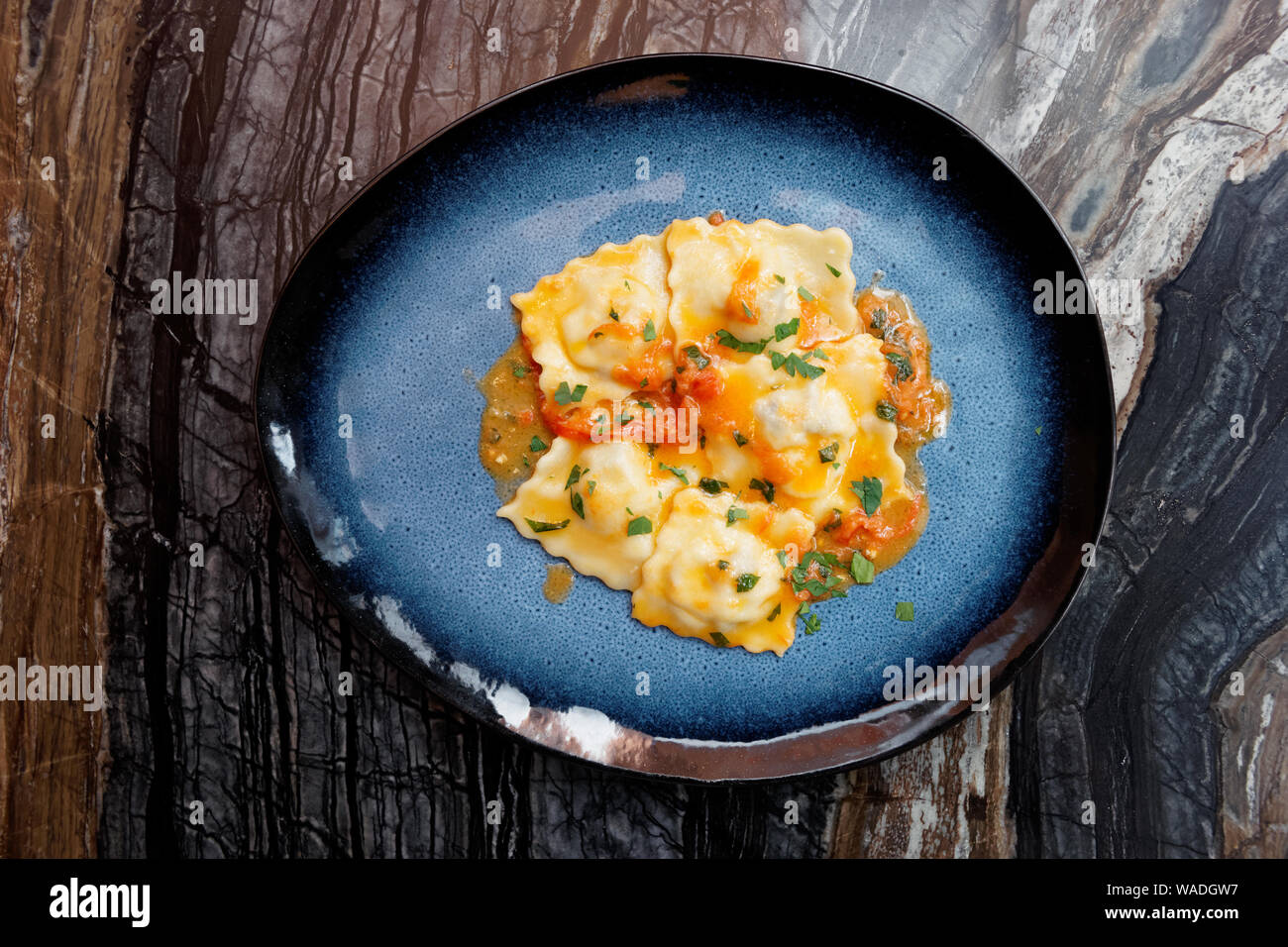 Ravioli in dark blue plate on marble table shot from above Stock Photo ...