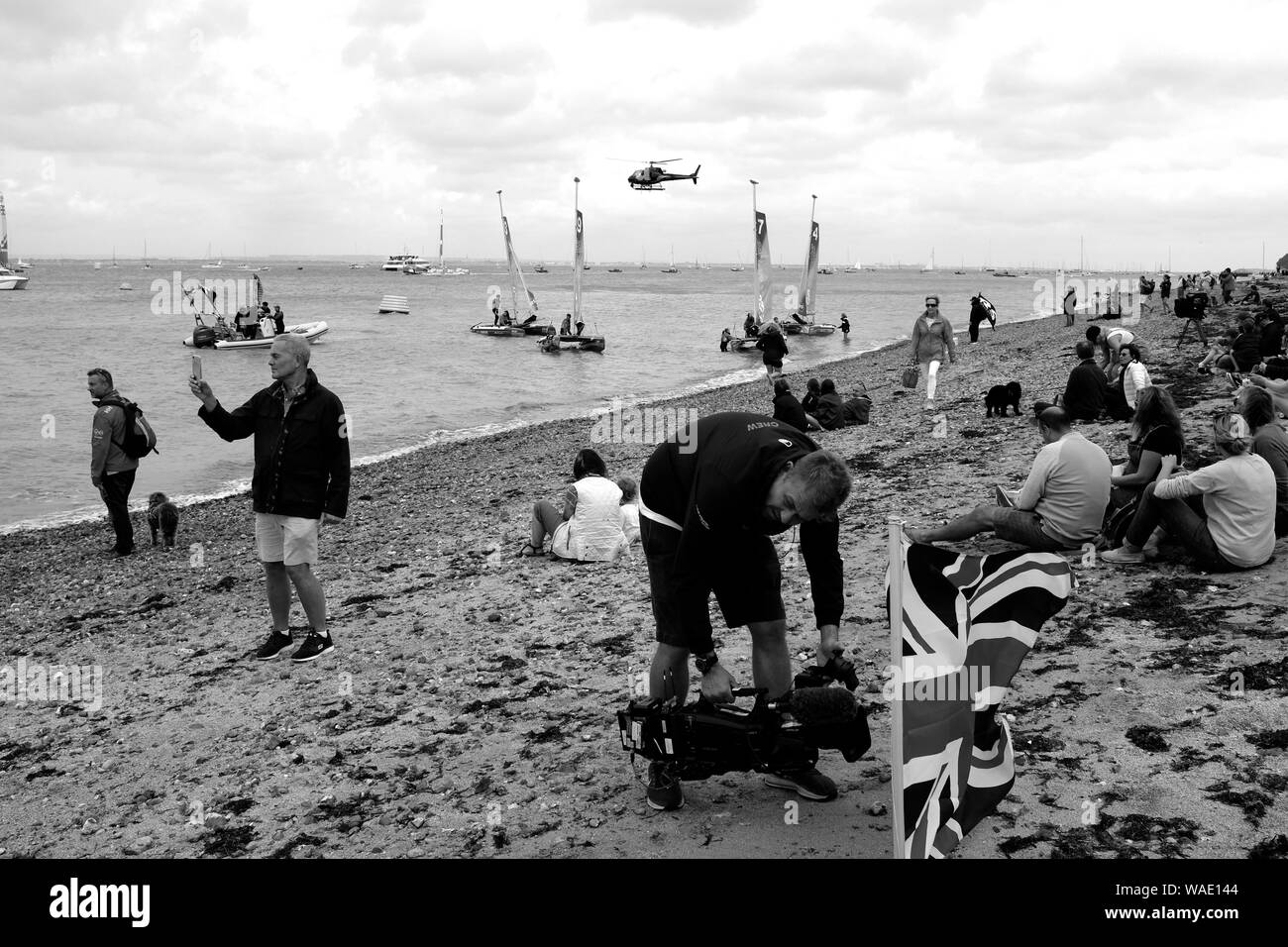 Crowds of spectators watching Cowes Week yacht racing from the beach at ...