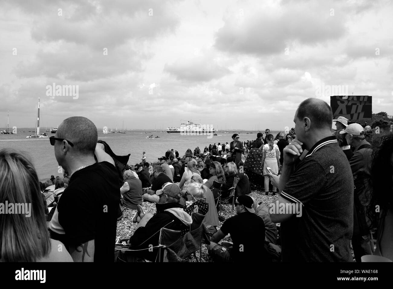 Crowds of spectators watching Cowes Week yacht racing from the beach at ...