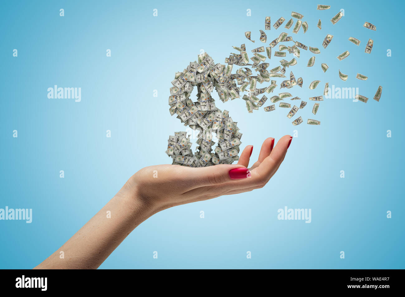 Female hand holding money dollar sign shattering on blue background ...