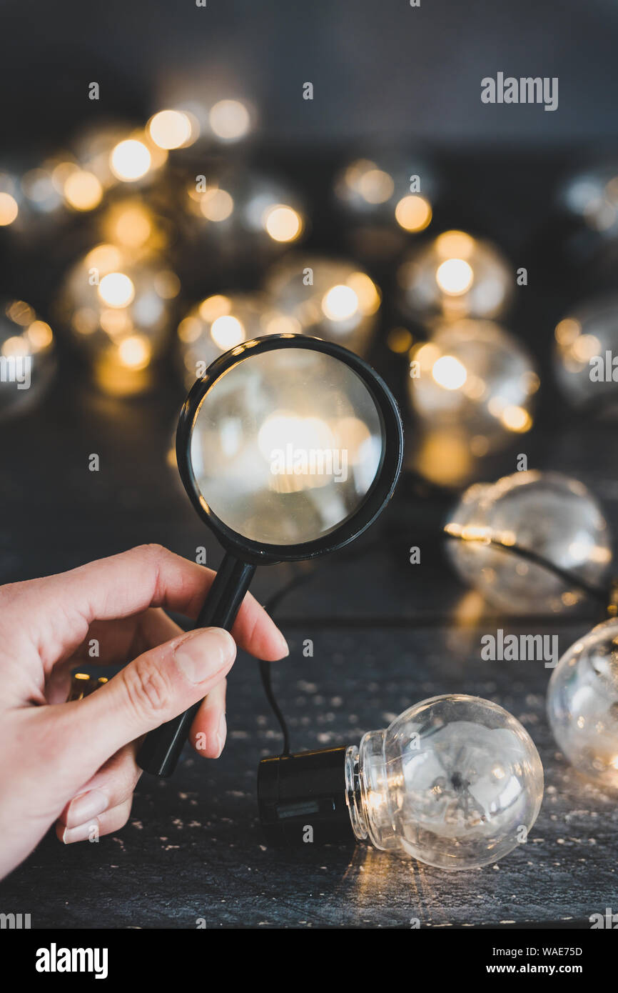 hand holding magnifying glass analyzing different ideas in shape of lightbulb string lights ...