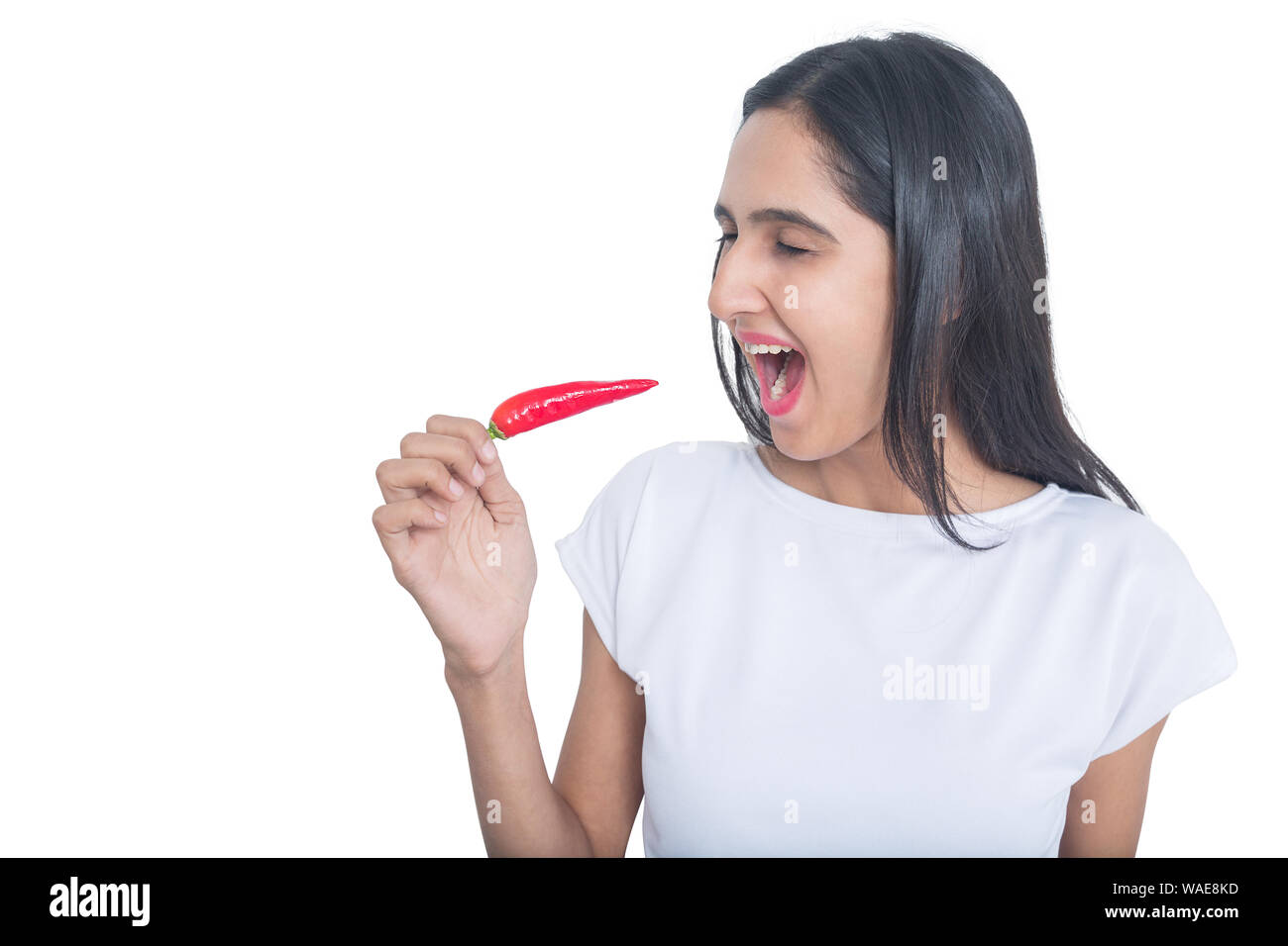 Beautiful girl trying to eat red pepper chilli isolated on white ...