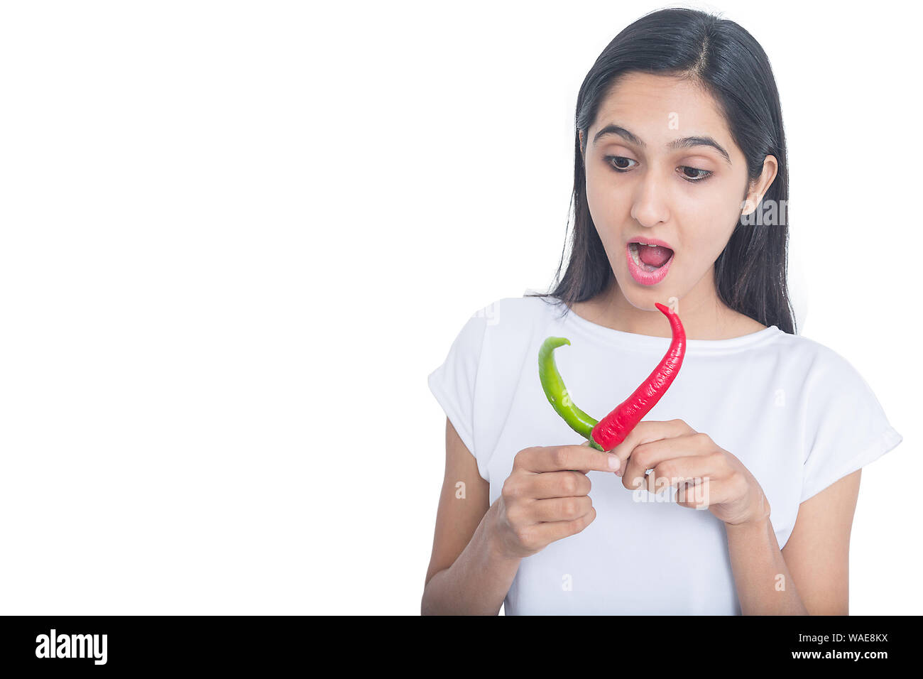 Young brunette girl holding red and green pepper chilli with surprised ...