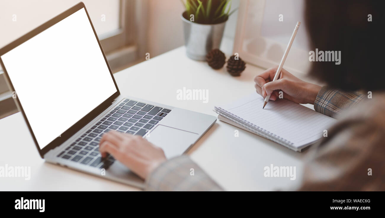 Young businesswoman typing on blank screen laptop computer and writing ...