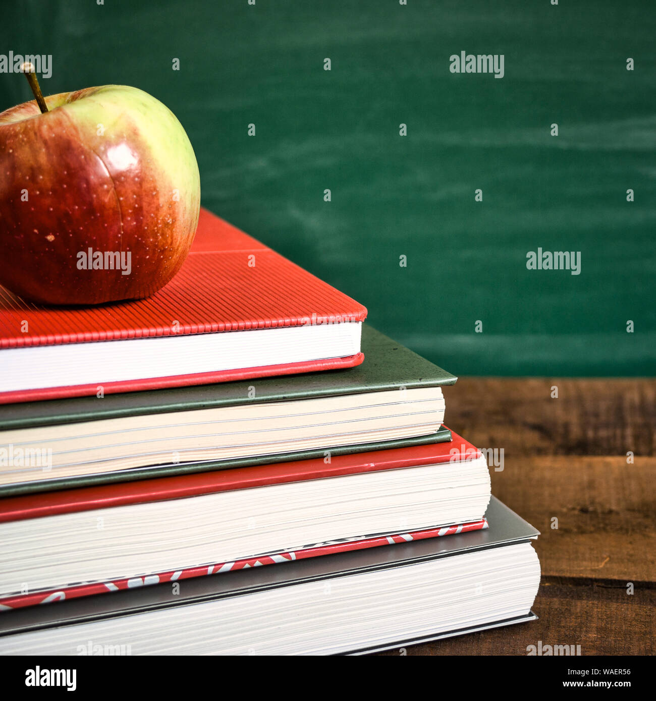 Books and apple on wooden table in front of the school chalkboard. Back ...