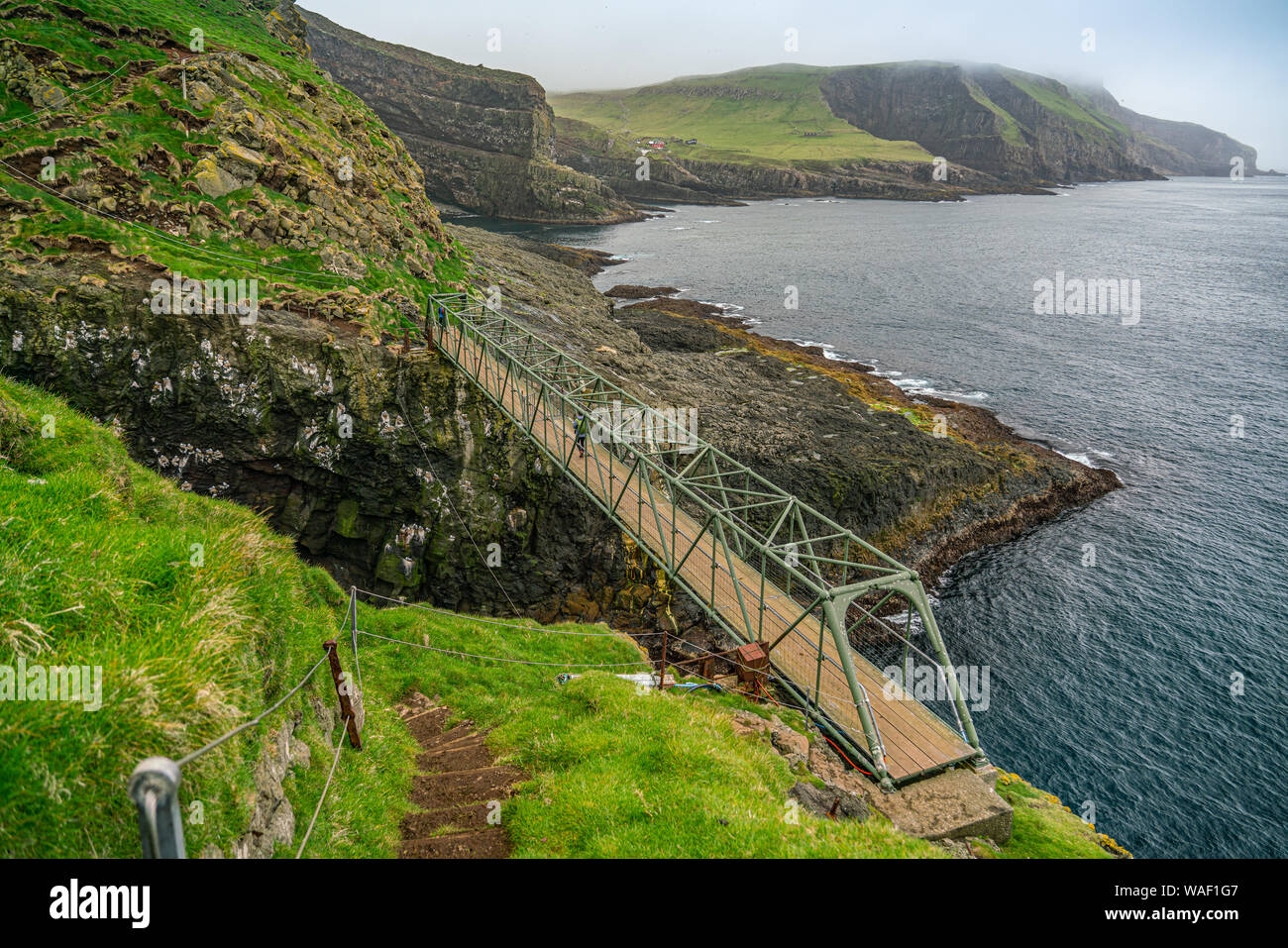 Unidentified tourist crossing the bridge in Mykines joining two sides ...
