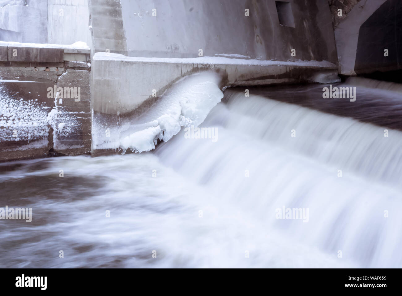 spillway of a small dam in winter with ice and snow on the concrete ...