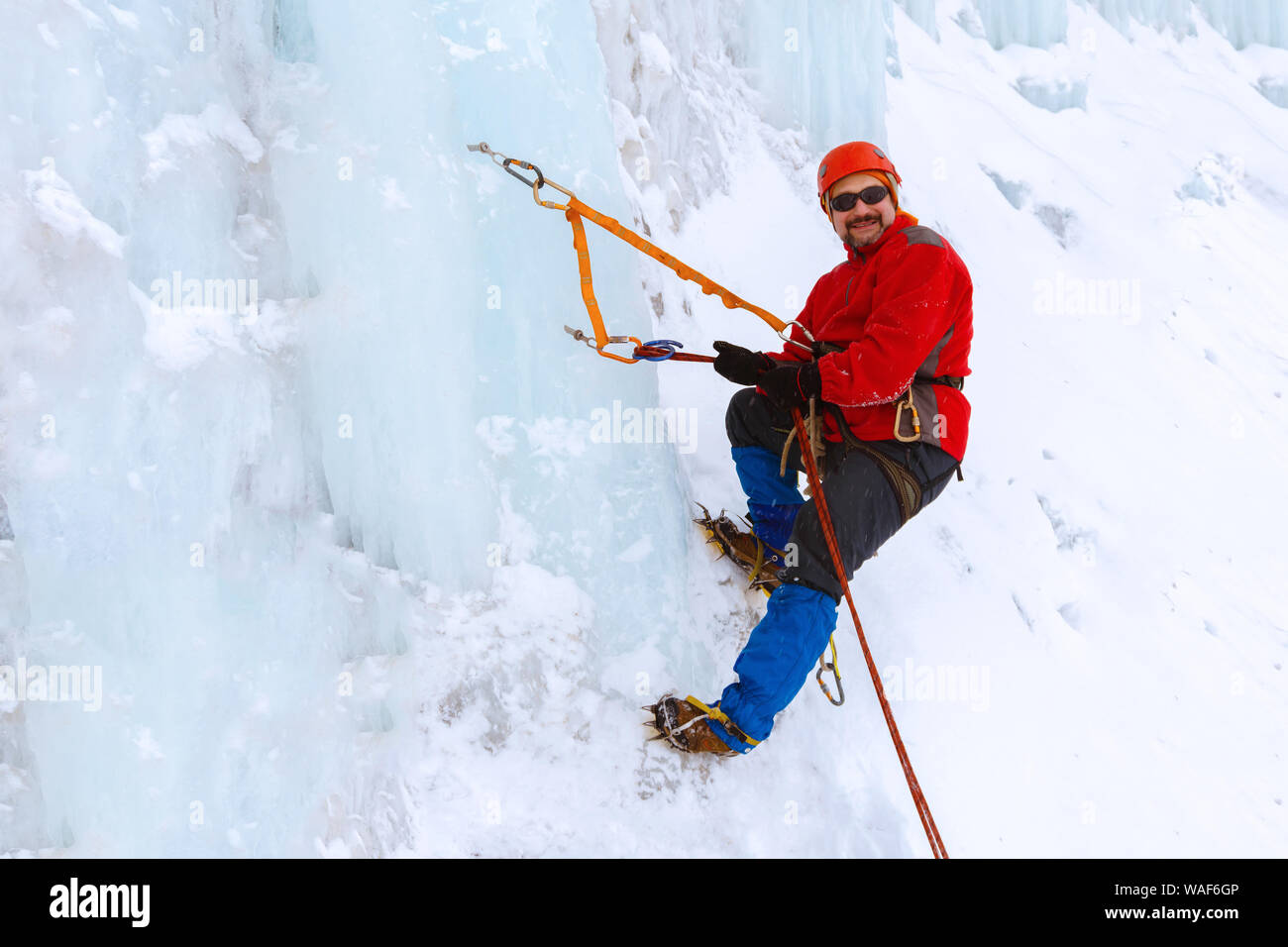 ice-climber with safety equipment makes an ascent on the ice wall of a ...