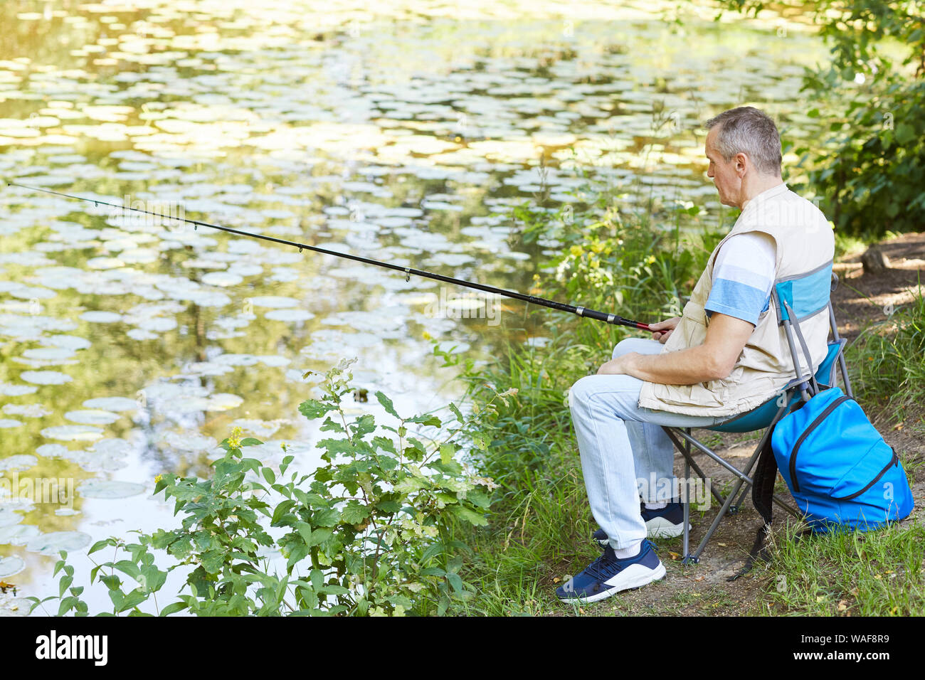 Mature fisherman sitting on chair with fishing rod he fishing at the ...