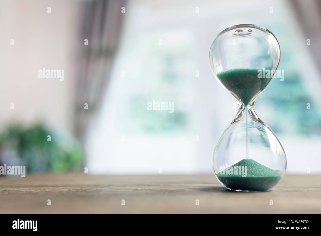 Hourglass time passing on table in room by window Stock Photo - Alamy