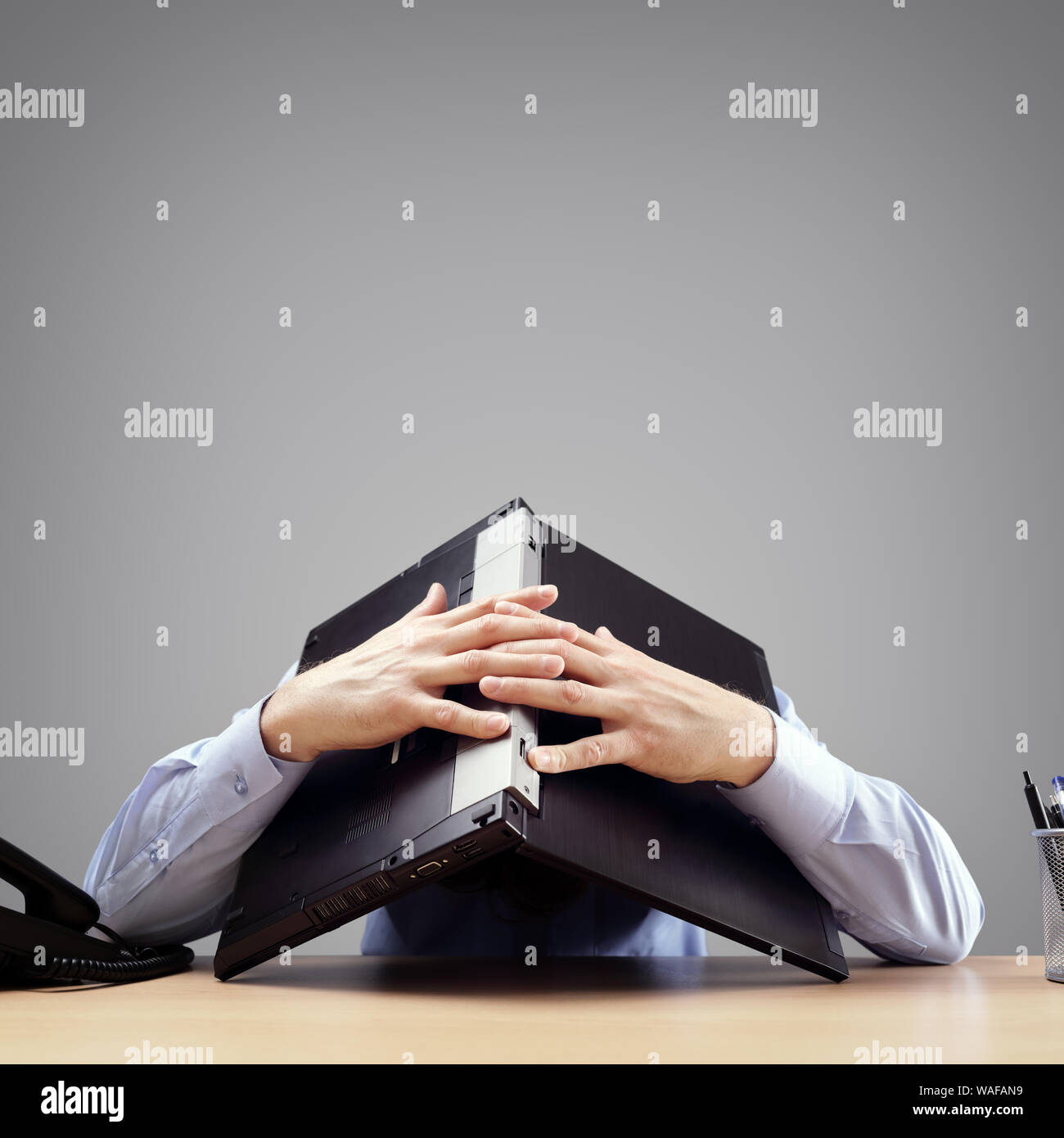 Frustrated and overworked businessman burying his head under a laptop ...