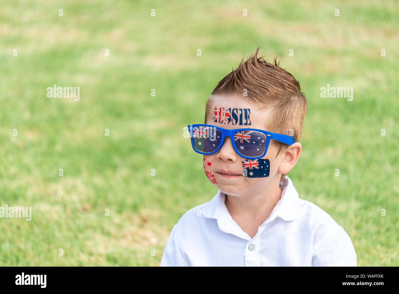 Smiling Australian boy with sunglasses sitting on lawn during Australia ...