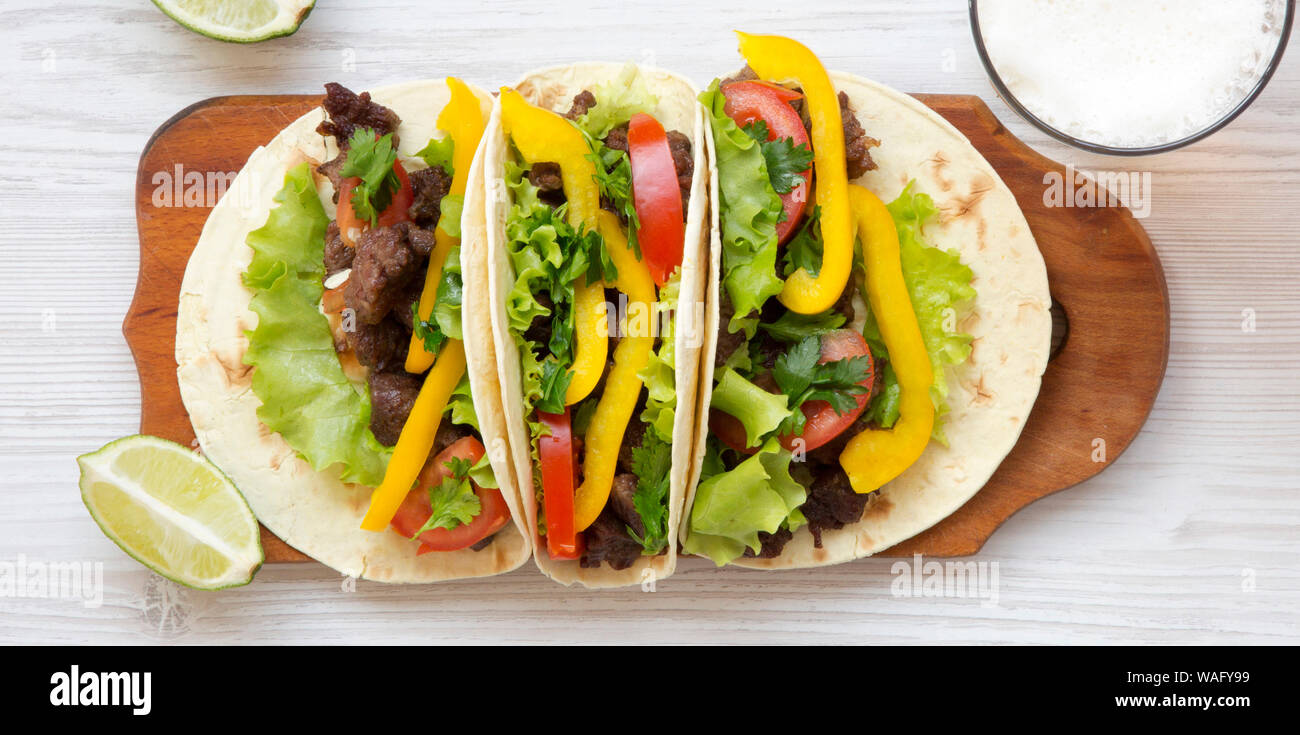 Tacos with pork, vegetables, avocado, lime and beer on a white wooden ...