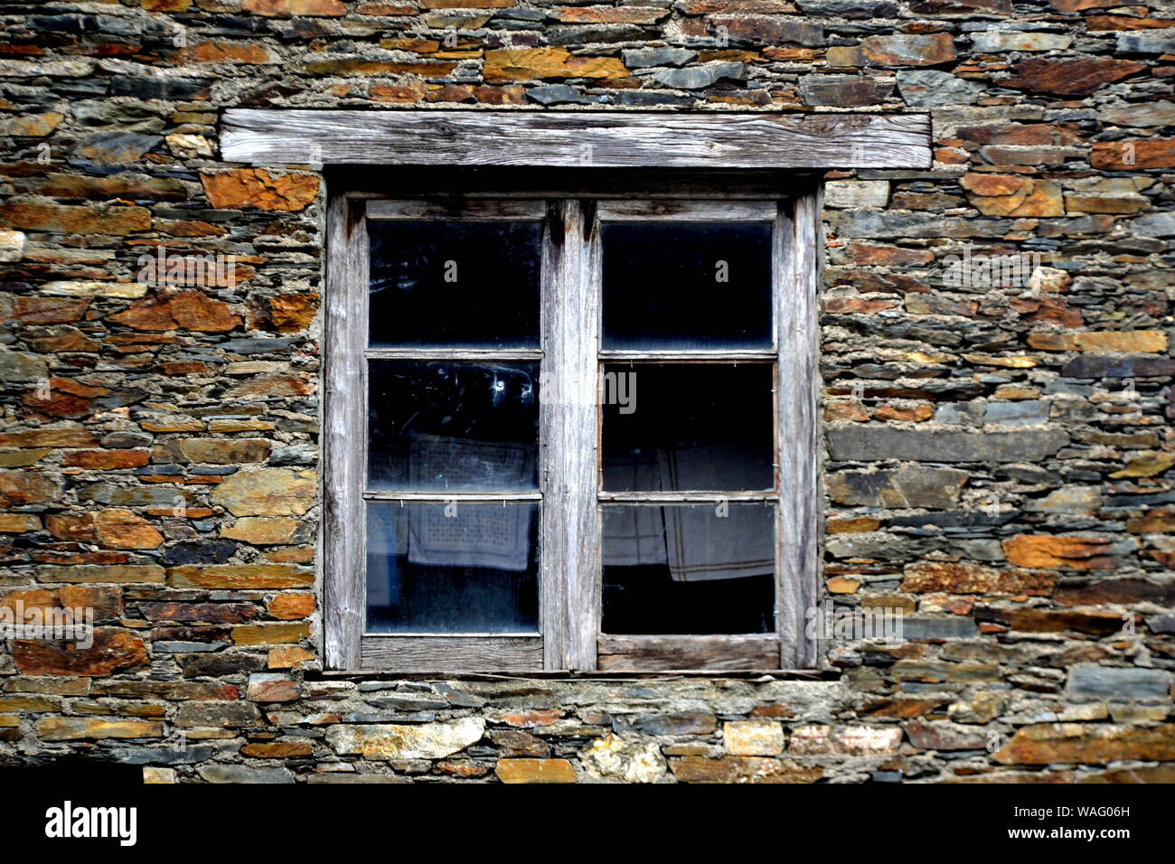 Rustic hand-hewn wood window set into a stone wall built from schist in ...