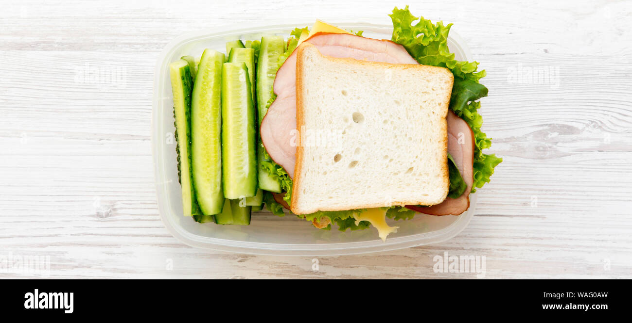 Lunch box with sandwich and vegetables on a white wooden surface, top ...