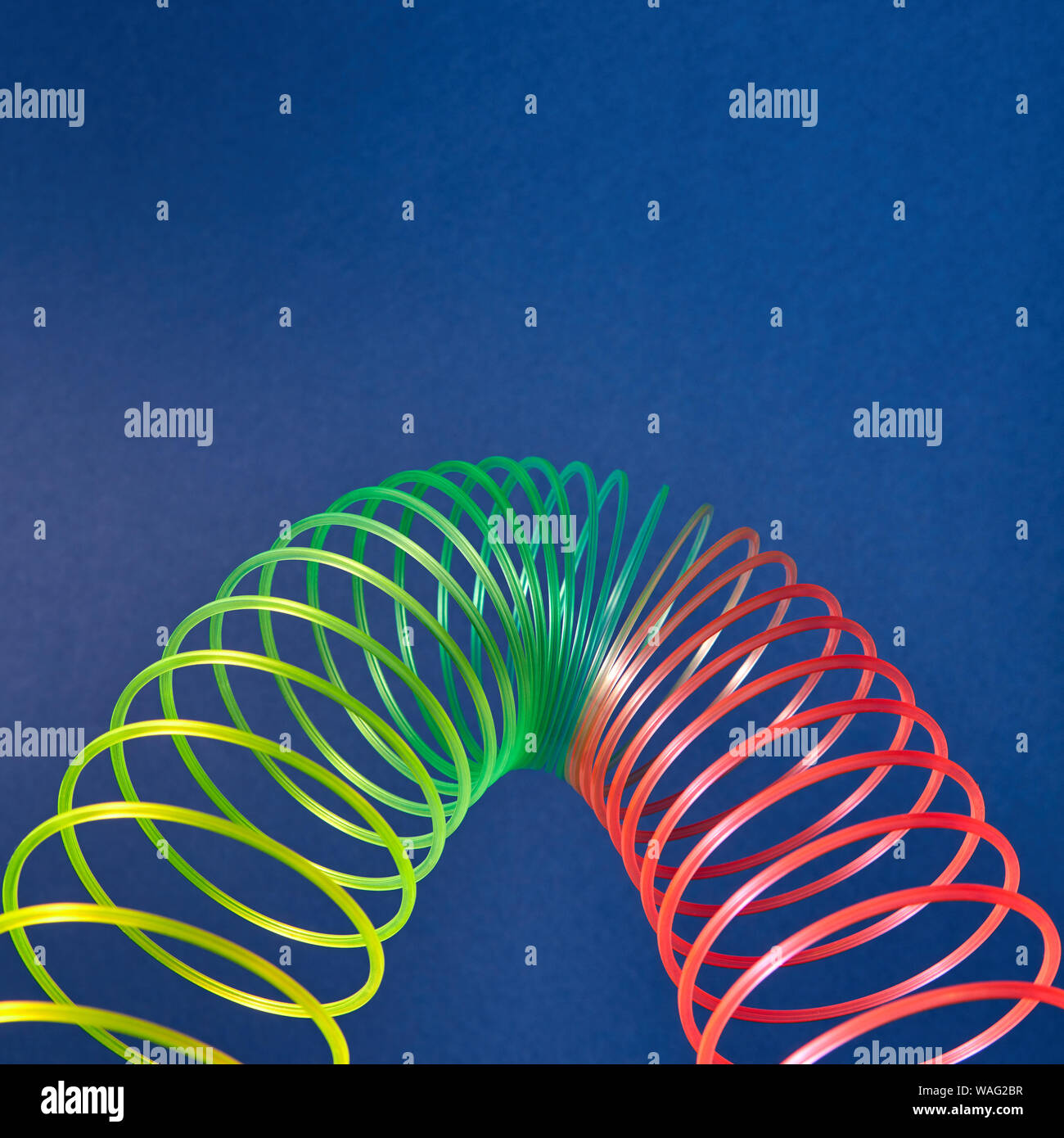 Flexible rainbow plastic spring in a form of parabola on a blue ...