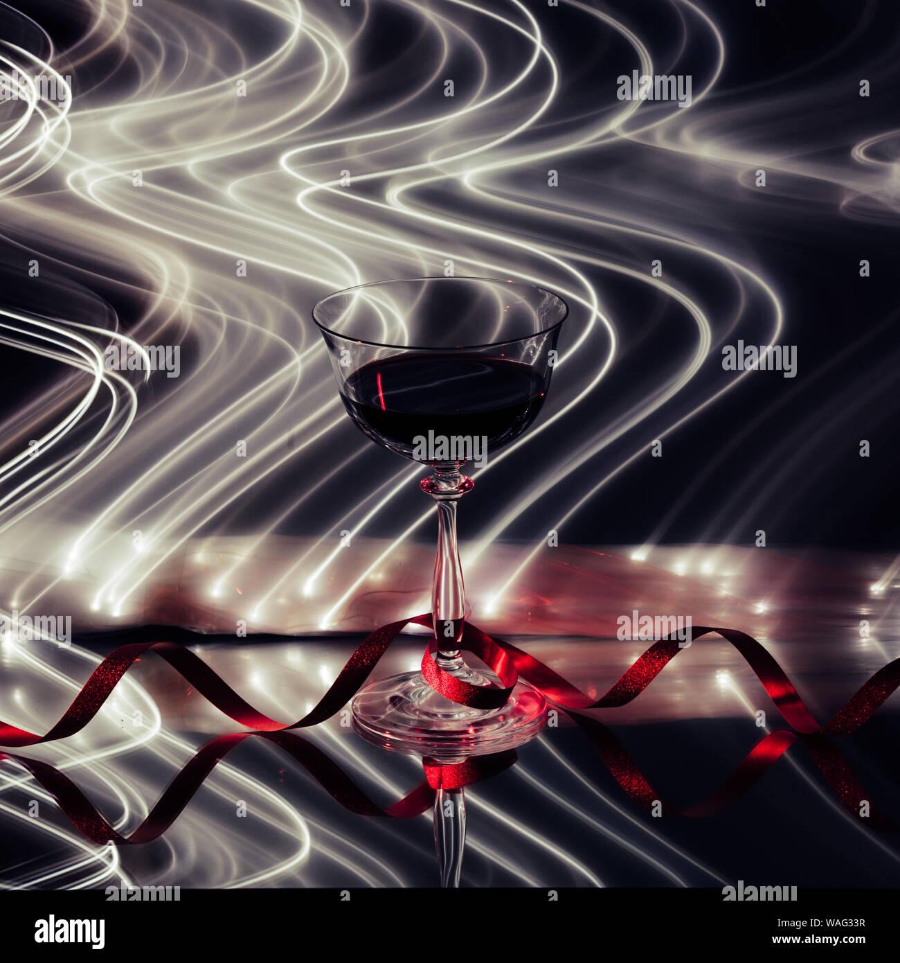A wine glass, with lines of lights in the background and a red ribbon ...