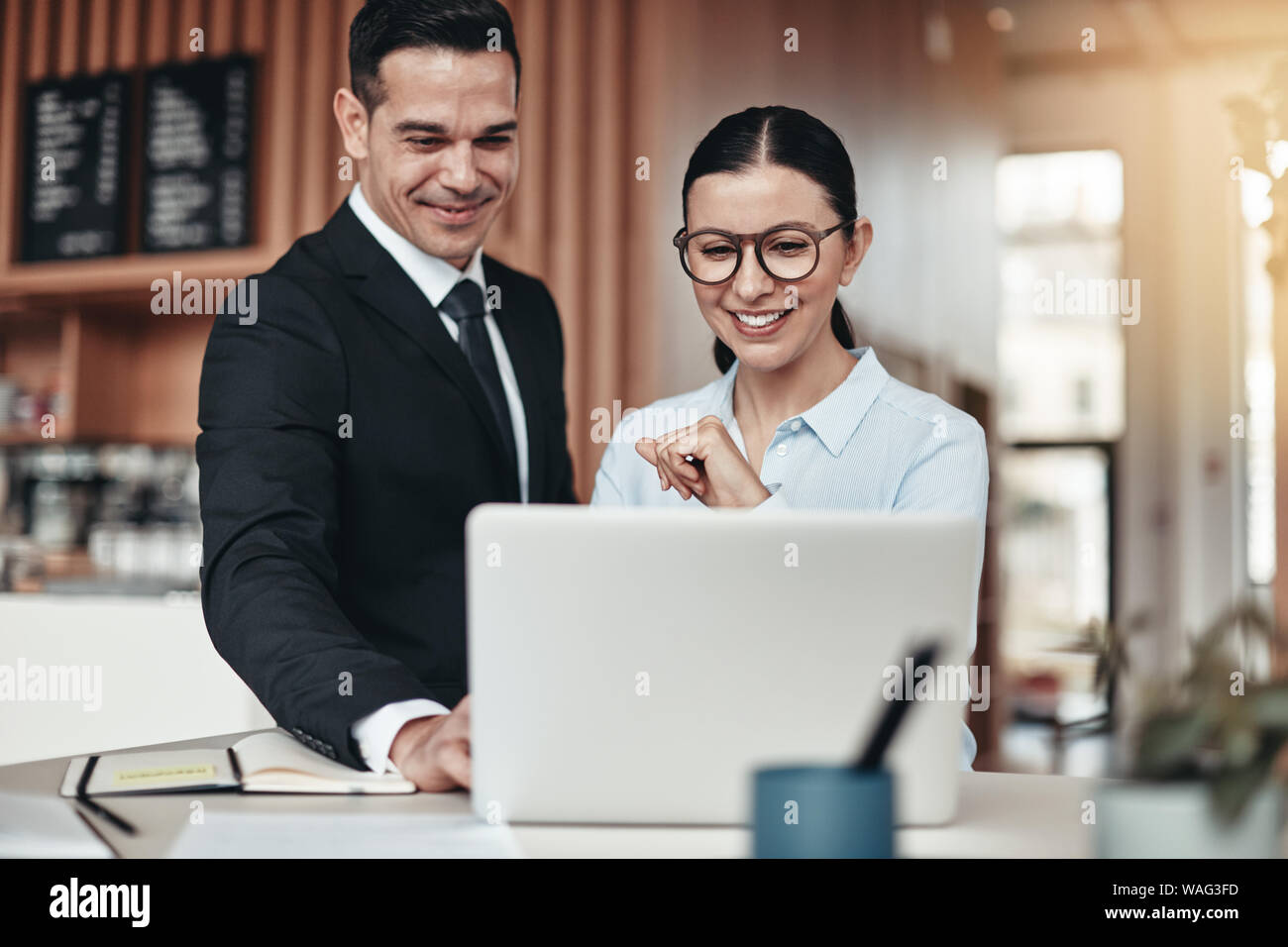 Two young work colleagues smiling while standing together at a table in ...