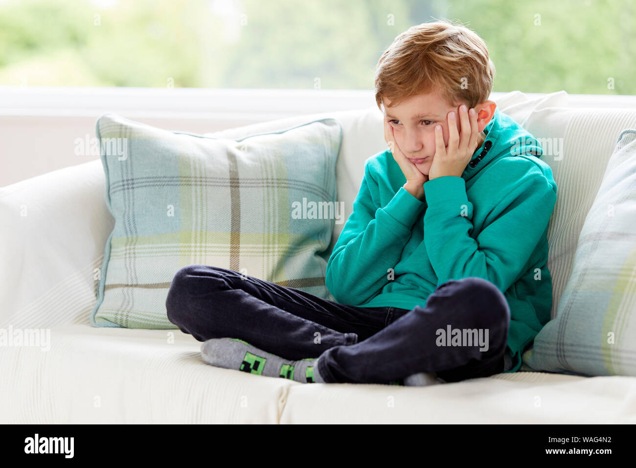 Boy looking depressed sat on a sofa Stock Photo - Alamy