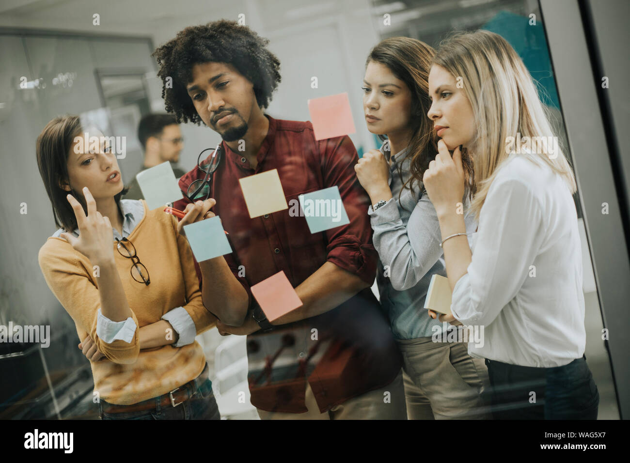 Group of young business people discussing in front of glass wall using ...