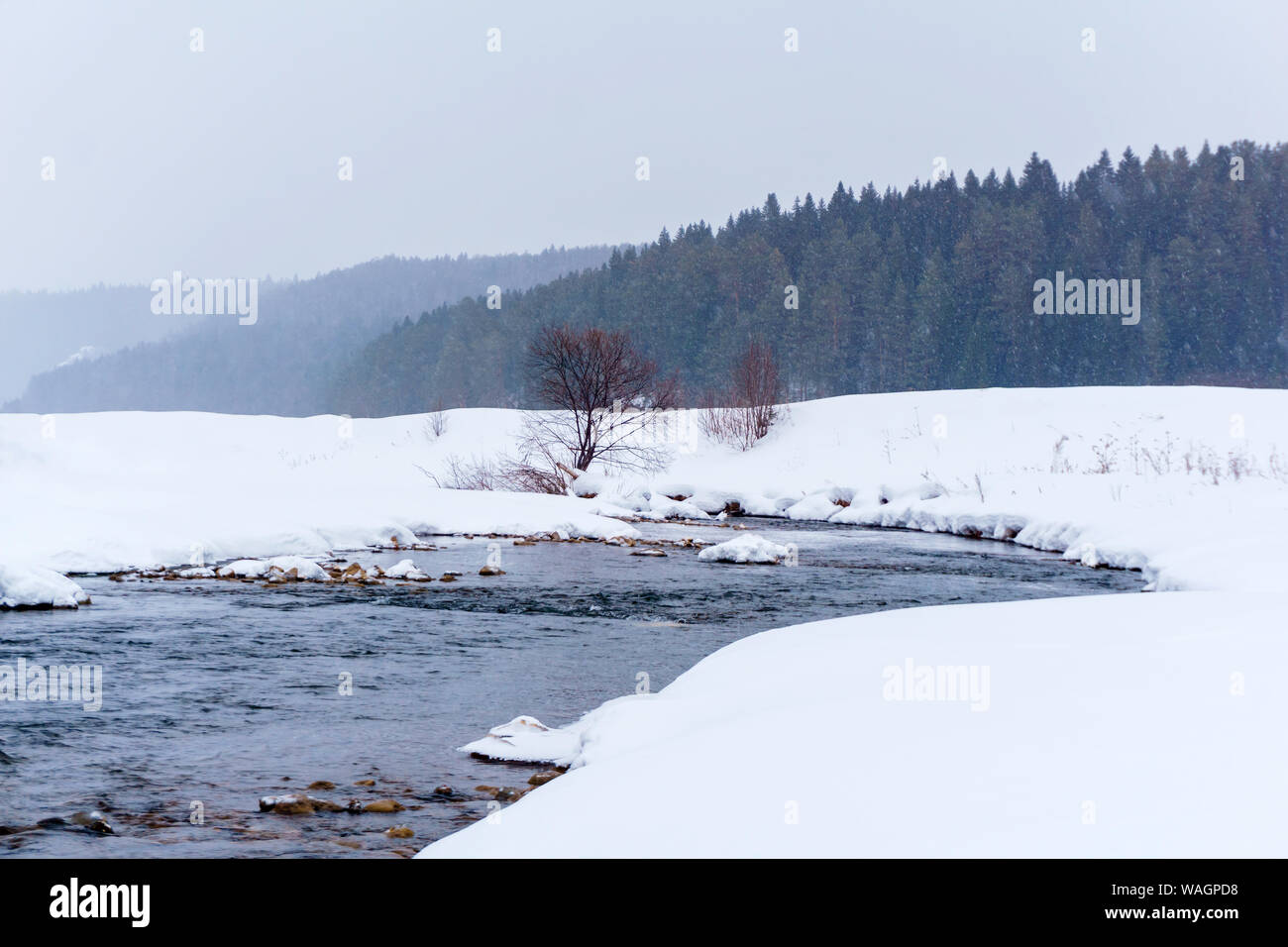 snowy March landscape in early spring, thawed out stream in a valley ...