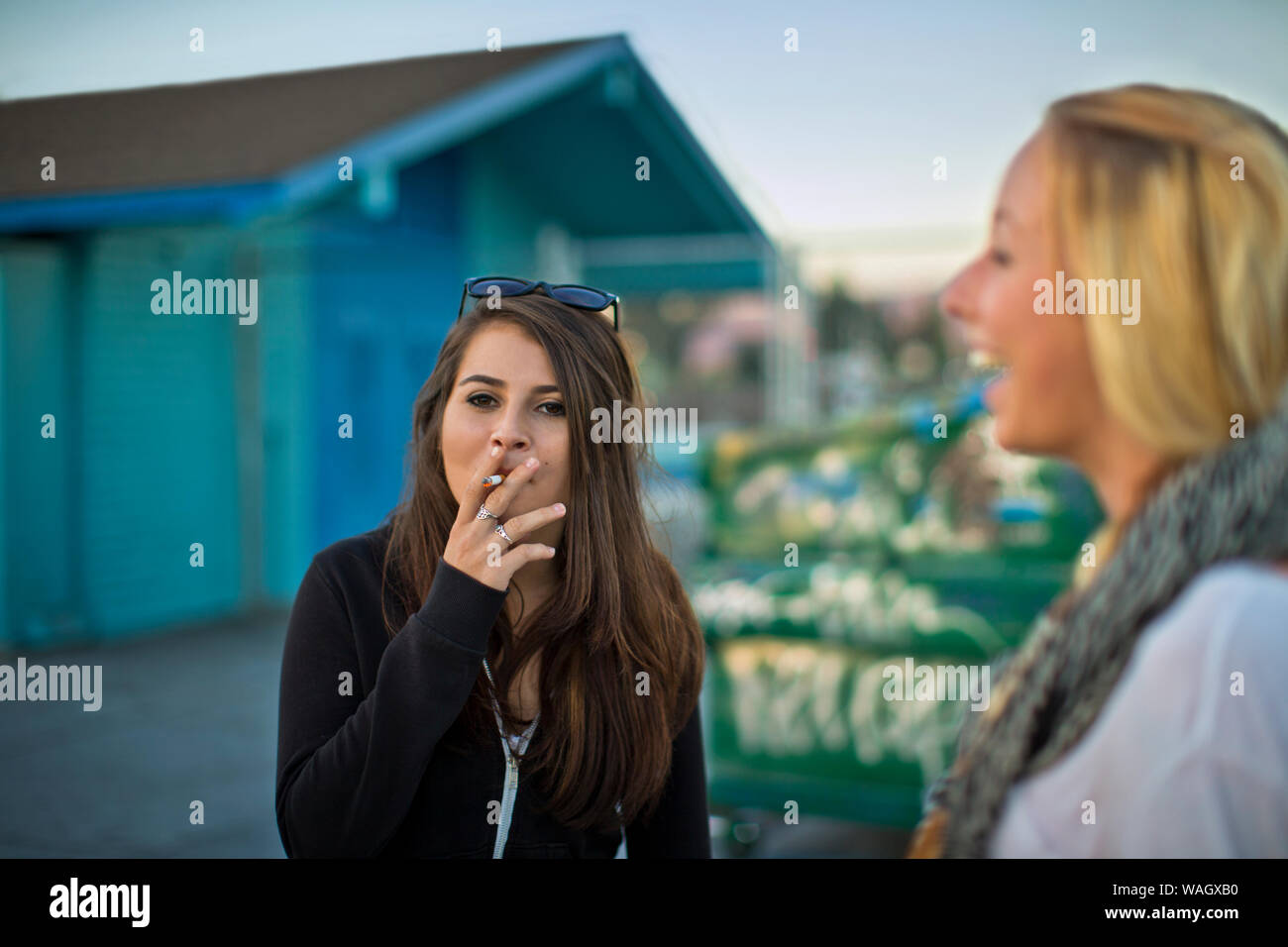Young adult woman smoking by dumpster Stock Photo - Alamy