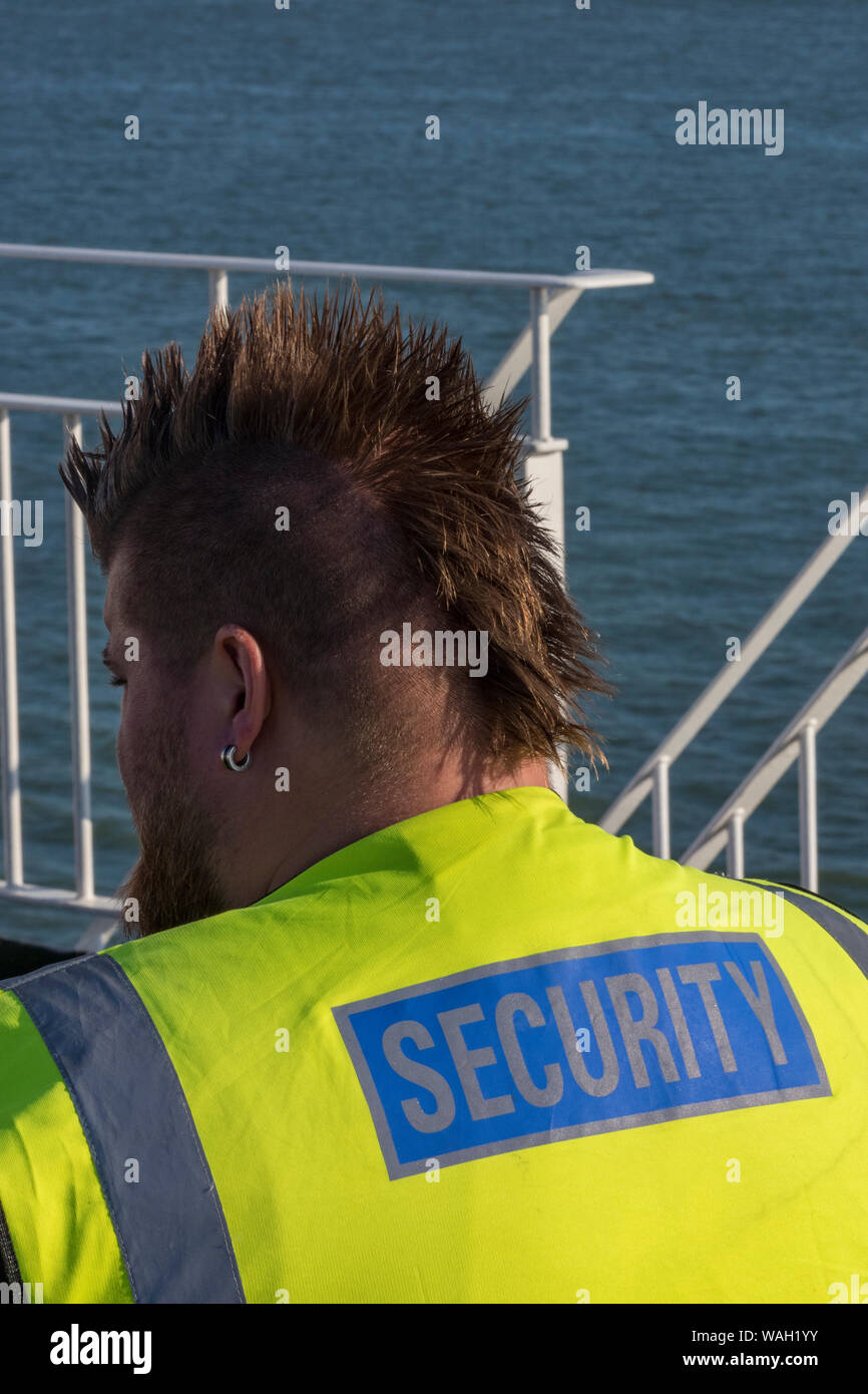 a security guard wearing a high visibility vest with spiky hair. tough ...