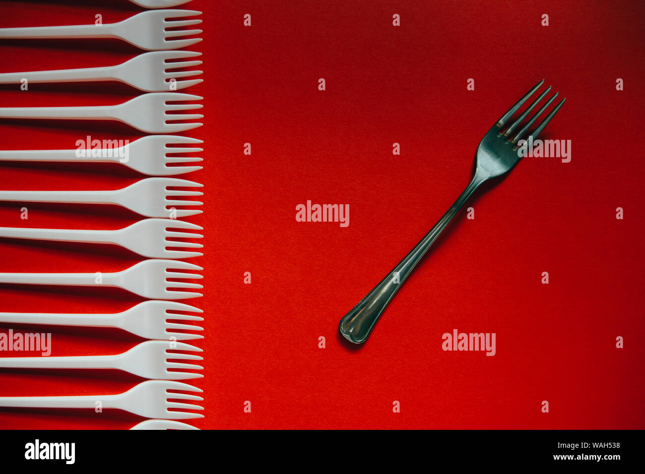 A lot of plastic forks vs a metal one on a red background. The concept ...
